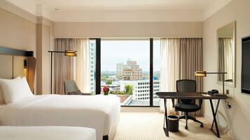 Quarto de hotel com duas camas, uma mesa, uma cadeira, televisão e vista para a cidade.