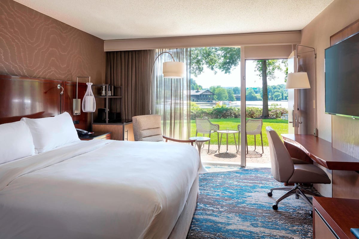 Quarto de hotel com uma cama grande, uma mesa com cadeira, TV e vista para um jardim por uma porta de correr.