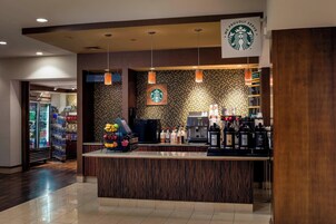 Uma cafeteria Starbucks com balcão de madeira, máquinas de café expresso e um quadro de menu.