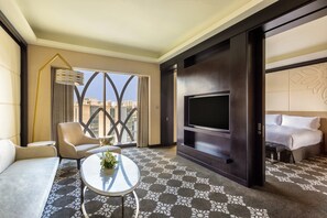 Quarto de hotel com sofá, poltrona, mesa de centro redonda, televisão e cama.
