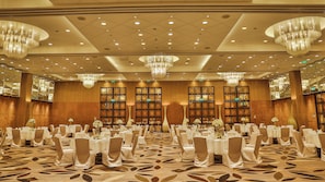 Uma sala de banquetes com mesas redondas, lustres e paredes espelhadas.