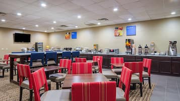 Uma área de restaurante com mesas e cadeiras, um espaço para café e um balcão com alimentos.