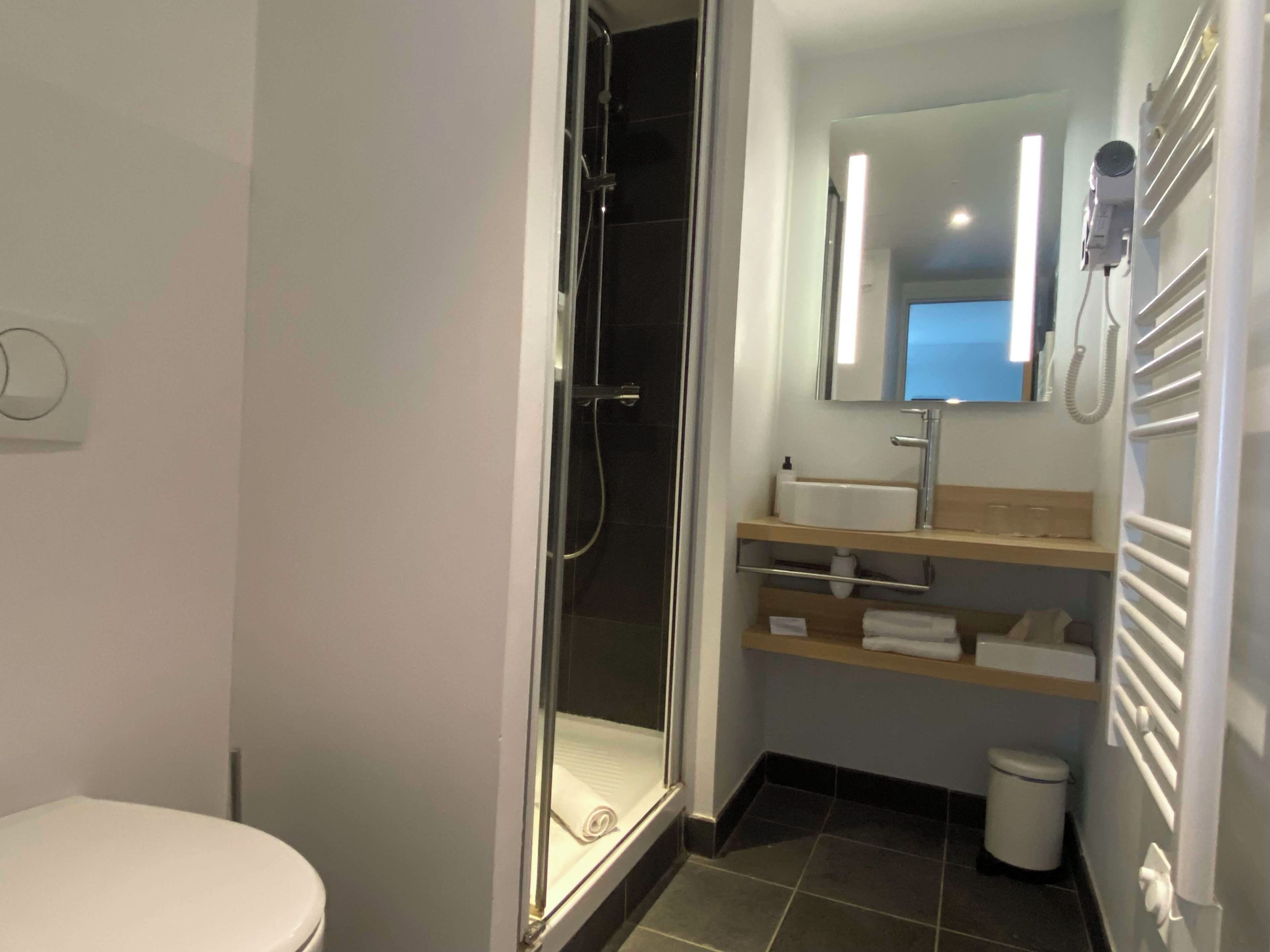 Casa de banho moderna com cabine de duche em vidro, sanita branca, lavatório com espelho e porta-toalhas.