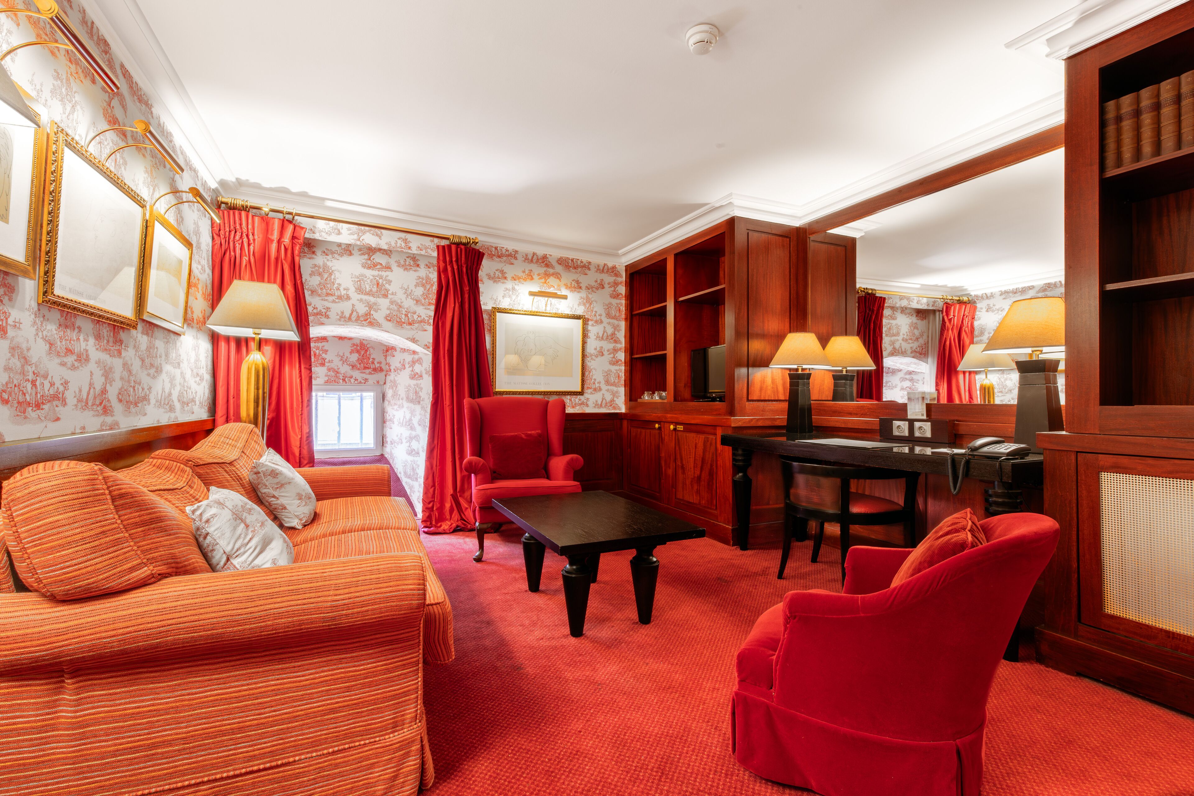 Quarto com sofá vermelho, poltrona vermelha, mesa de centro de madeira e estante de livros.
