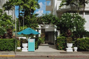 Entrada de hotel com placa, caminho e vegetação exuberante.