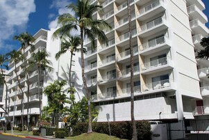 Um hotel com vários andares, varandas, palmeiras e um céu claro.