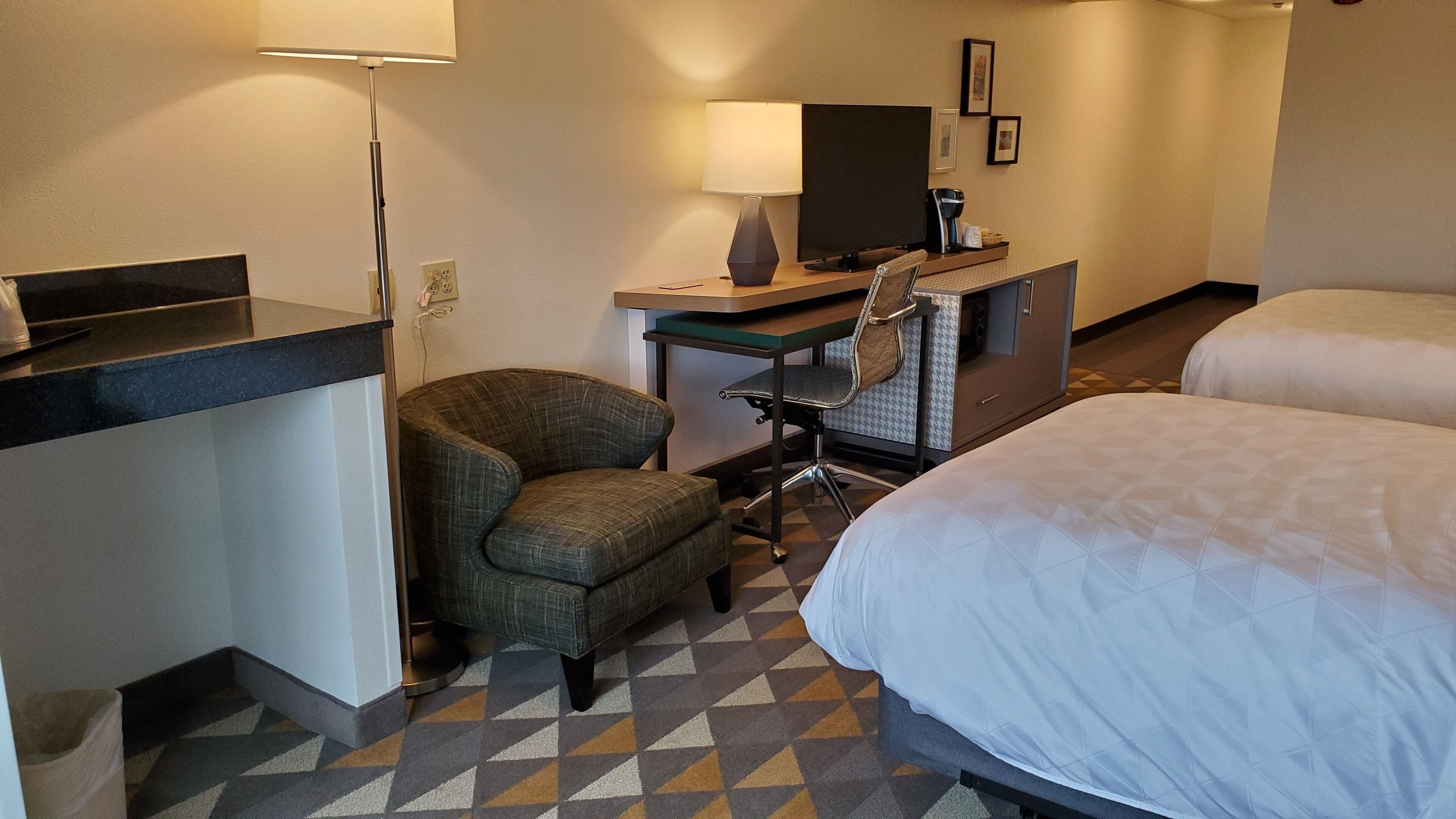 Quarto de hotel com escrivaninha, cadeira, duas camas e televisão.