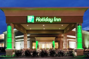 Entrada de um hotel Holiday Inn com uma placa verde chamativa, colunas e fachada bem iluminada.