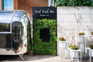 Um bar tipo food truck chamado Barceló Imagine, com uma parede verde e vasos brancos.