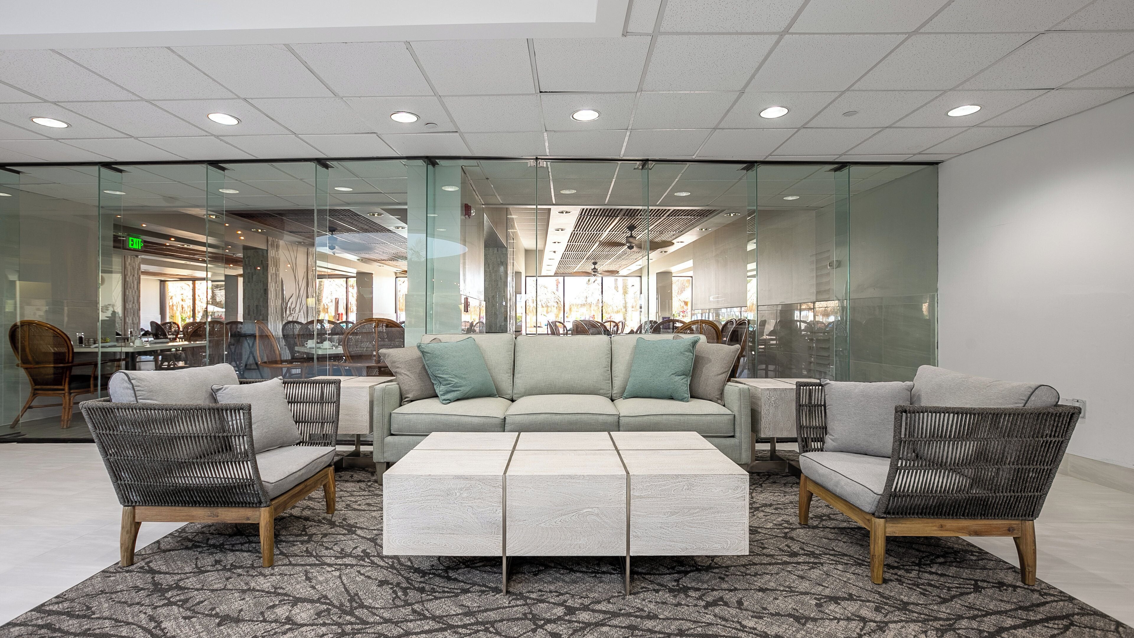 Um lobby moderno com um sofá de canto, duas poltronas, uma mesa de centro e um tapete estampado.