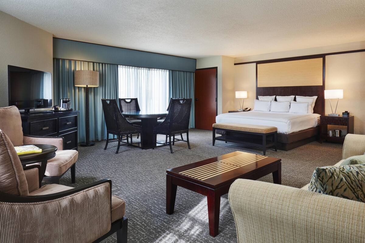 Quarto de hotel com cama, escrivaninha, cadeira, cafeteira, luminária e televisão.