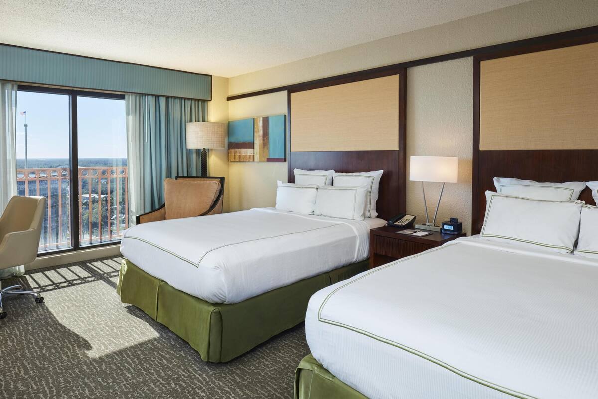 Quarto de hotel com duas camas, uma escrivaninha, uma cadeira e vista para a cidade.