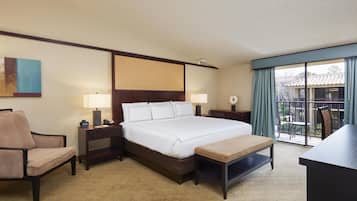 Quarto de hotel com cama, mesas de cabeceira, uma cadeira, um banco, uma escrivaninha e vista para o exterior.
