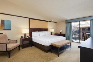 Quarto de hotel com cama, mesas de cabeceira, uma cadeira, um banco, uma escrivaninha e vista para o exterior.