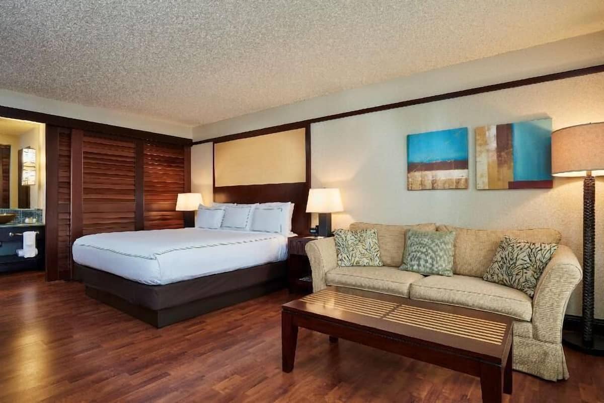 Quarto de hotel com cama, sofá, mesa de centro e obras de arte na parede.