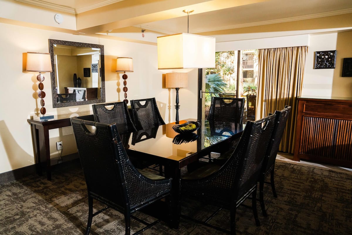 Uma sala de jantar com mesa, cadeiras, espelho, luminárias e vista para o exterior.