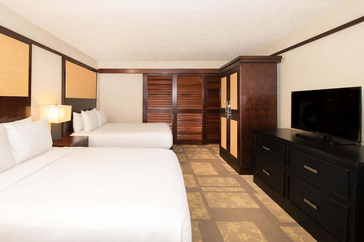 Quarto de hotel com duas camas, televisão, cómoda e porta para um armário.