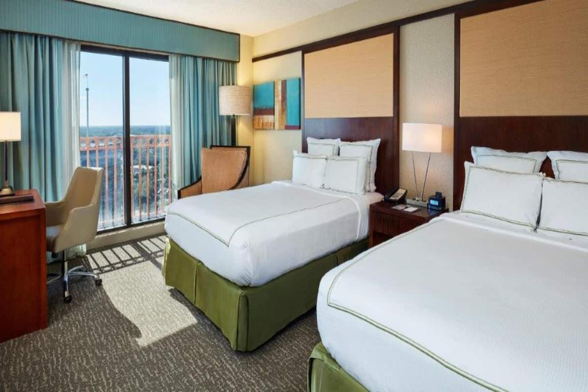 Quarto de hotel com duas camas, uma escrivaninha, uma cadeira e vista para a cidade.