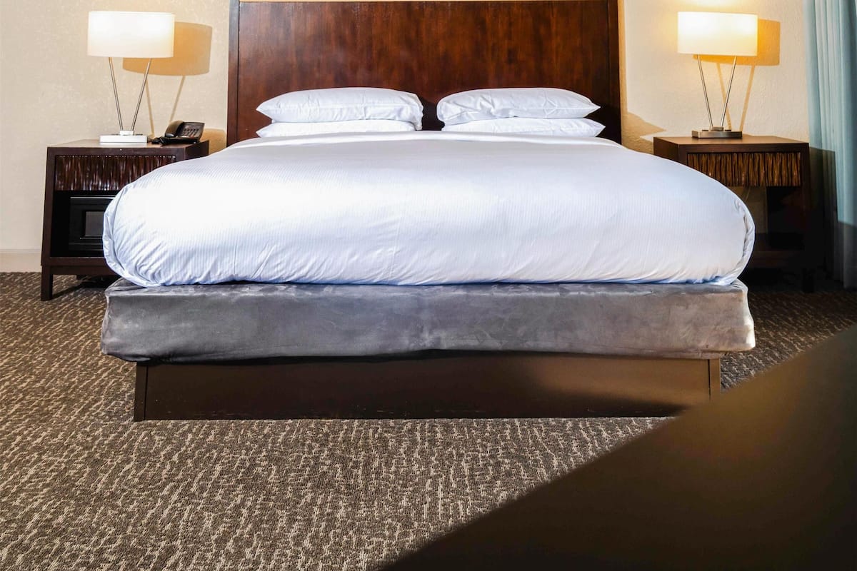 Quarto de hotel com uma cama grande, duas mesas de cabeceira, cabeceira e uma televisão.