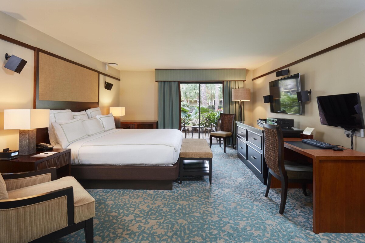 Quarto de hotel com uma cama grande, uma escrivaninha com computador, televisão e vista para o exterior.