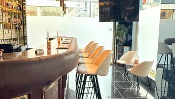 Uma área de bar moderna com balcão curvo, banquetas e uma televisão na parede.