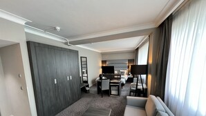 Quarto de hotel moderno com sofá, escrivaninha, televisão e guarda-roupa.