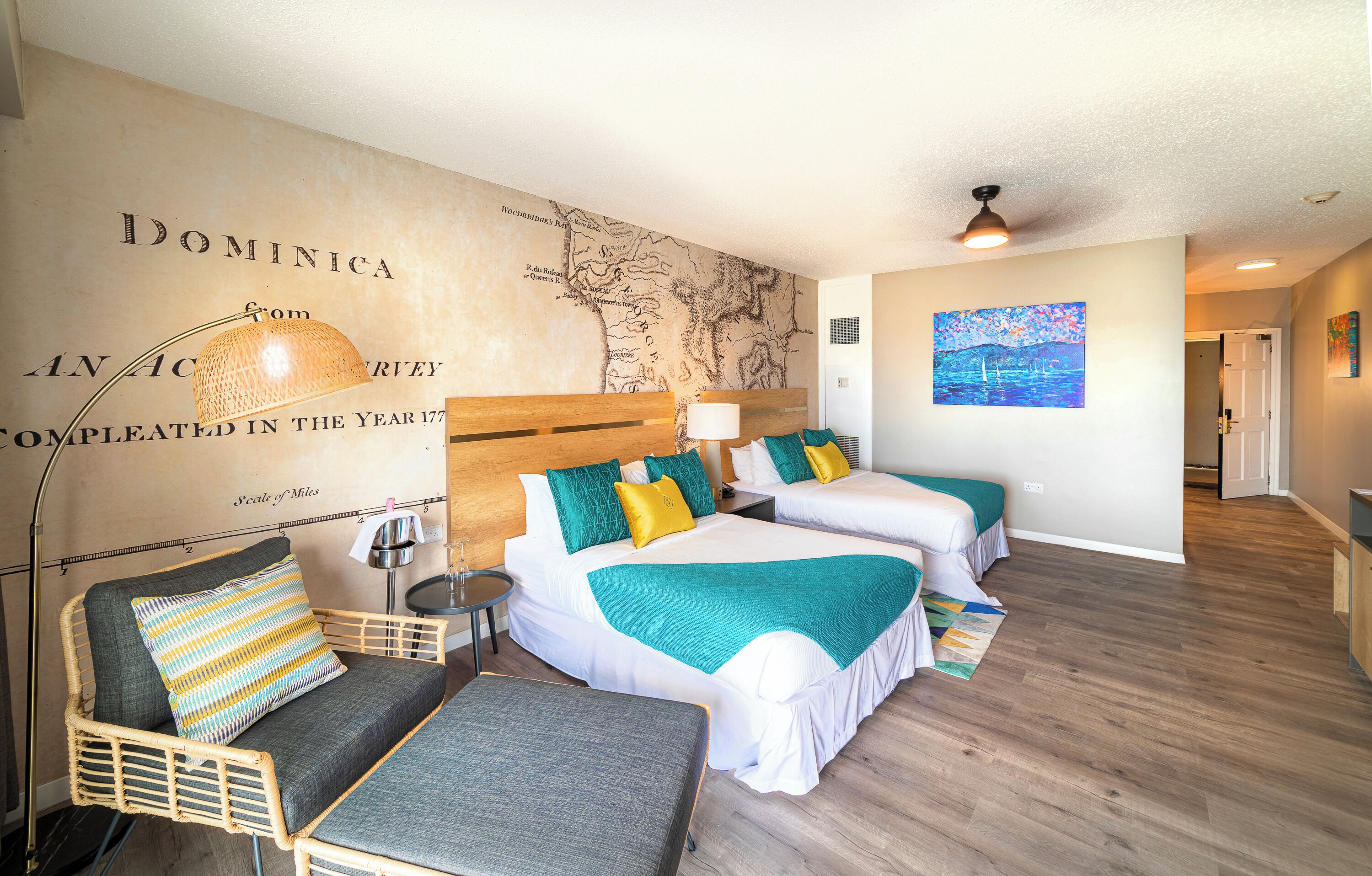 Quarto de hotel com duas camas, parede decorada com mapa, um quadro e uma cadeira de vime.