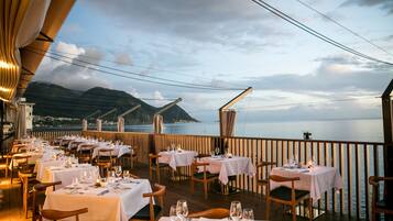 Restaurante com mesas preparadas para refeições, com vista para um corpo de água e uma montanha.