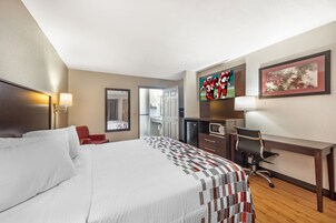 Quarto de hotel com uma cama grande, uma escrivaninha, uma cadeira, uma televisão e um quadro pendurado na parede.