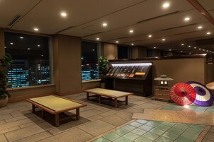 Um saguão de hotel com balcão de recepção, área de estar e grandes janelas com vista para a cidade.