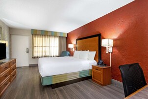 Quarto de hotel com uma cama grande, uma escrivaninha com telefone, uma cadeira, televisão e um guarda-roupa.