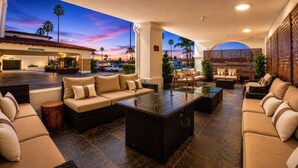 Uma área de estar externa ampla, com assentos confortáveis, uma mesa de centro grande e vista para o horizonte da cidade ao entardecer.