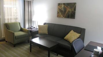 Quarto de hotel com uma poltrona verde, um sofá cinzento, uma mesa de centro e um quadro na parede.