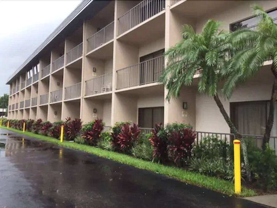 Um hotel com vários andares, varandas e um jardim bem cuidado com plantas tropicais.