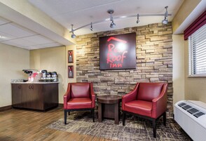 Lobby de um Red Roof Inn com parede de pedra, duas poltronas de couro, uma estação de café e uma placa.