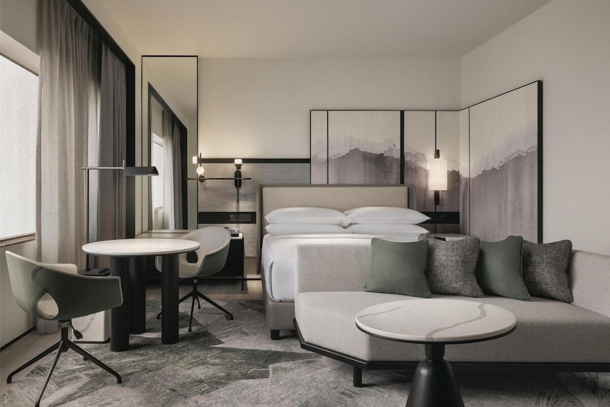 Quarto de hotel moderno com cama, sofá, mesa redonda, cadeira e escrivaninha.