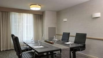 Sala de conferência com uma mesa comprida, quatro cadeiras e uma mesinha lateral com copos e uma planta.