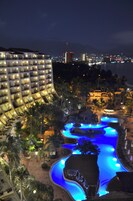 Um hotel com vários andares, piscina e palmeiras.
