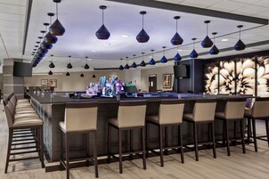 Uma área de bar com um balcão longo, vários bancos altos e iluminação pendente.