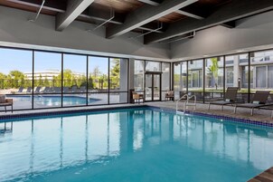 Piscina interior moderna com paredes de vidro transparente, espreguiçadeiras e vista para os arredores.
