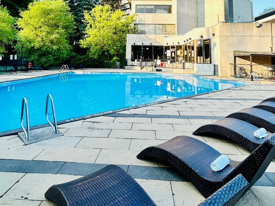Piscina com cadeiras de descanso e um edifício ao fundo.