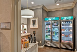 Uma suíte de hotel com minibar, um aviso para a loja da suíte e duas geladeiras Homewood Suites abastecidas com bebidas e petiscos.