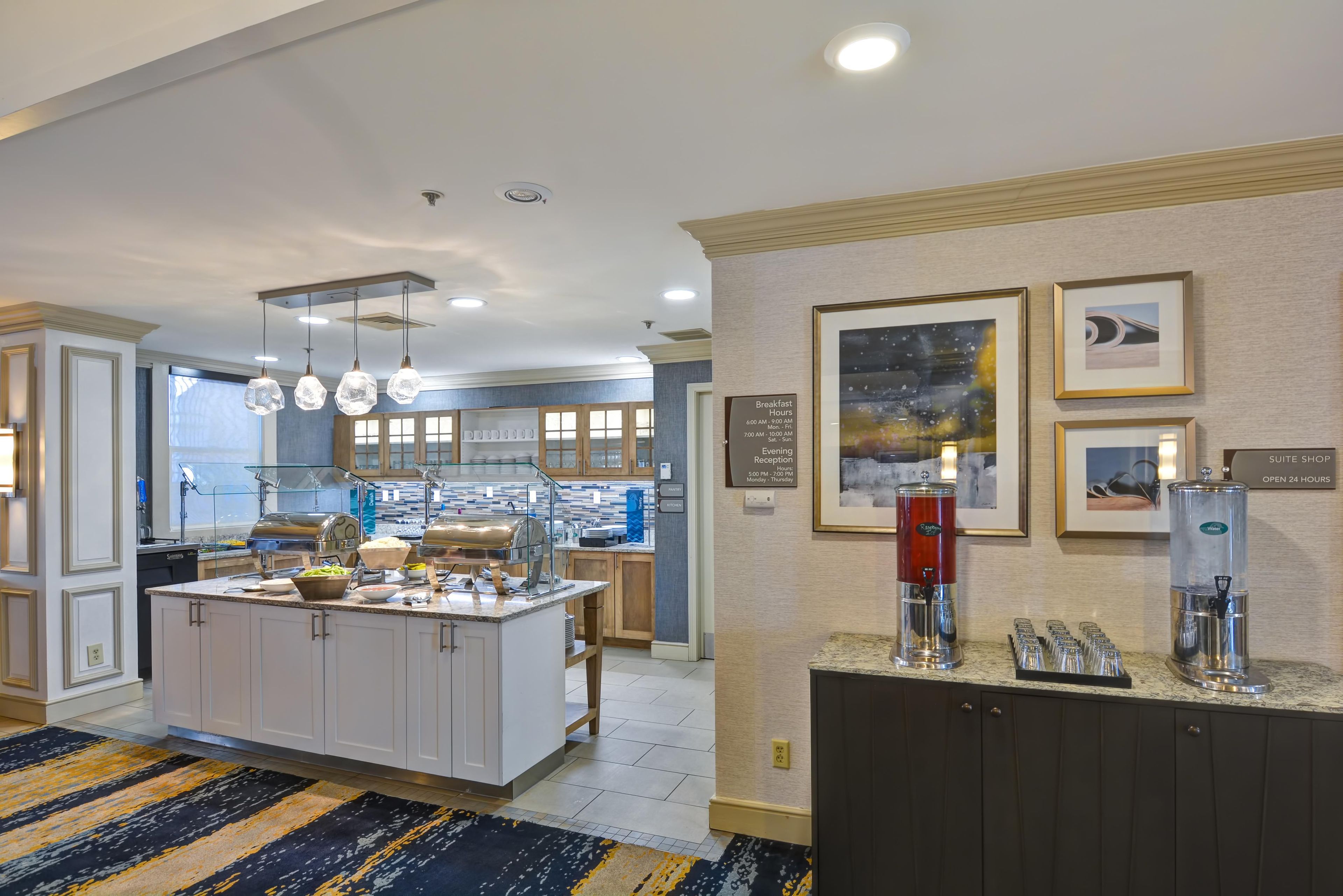 Cozinha de hotel com buffet, estação de café e aviso com os horários do café da manhã.
