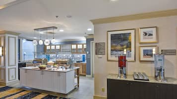 Cozinha de hotel com buffet, estação de café e aviso com os horários do café da manhã.