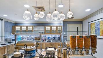 Disposição de buffet com diversos distribuidores de alimentos, um espaço para café e um balcão com pratos e talheres.