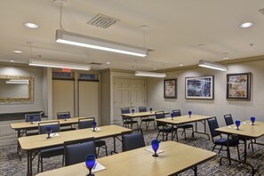 Uma sala de conferências com várias mesas, cadeiras e iluminação no teto.