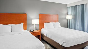 Quarto de hotel com duas camas, uma mesinha de cabeceira com abajur e vista para o exterior.
