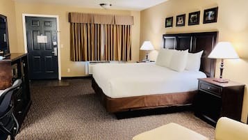 Quarto de hotel com uma cama, duas mesas de cabeceira com abajures, uma escrivaninha com cadeira, uma porta e piso coberto por carpete.