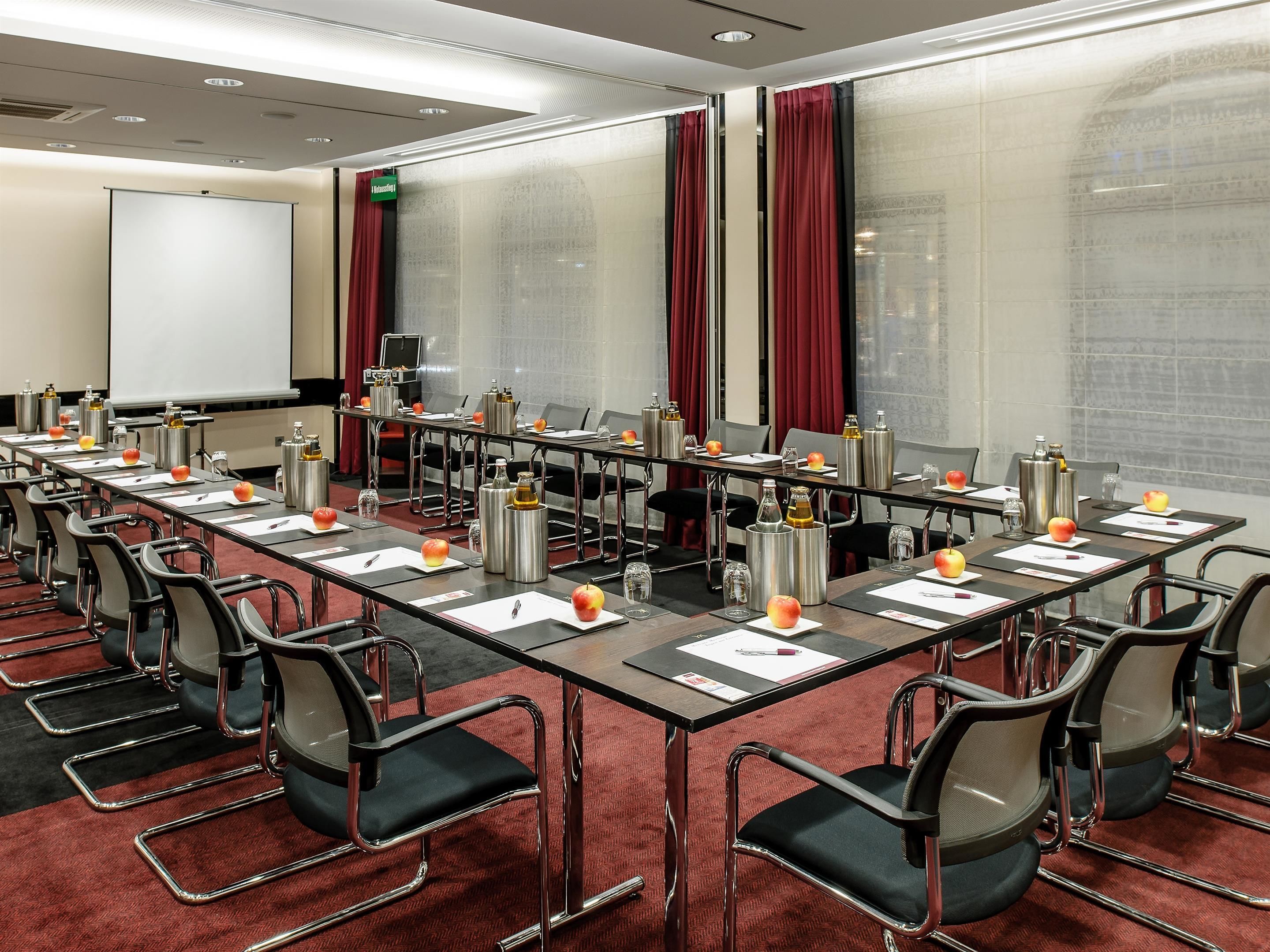 Uma sala de conferência com mesas compridas, cadeiras e telas de apresentação.