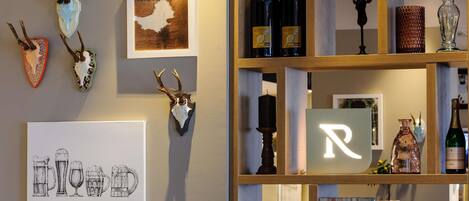 Paredes decoradas com caveiras de animais, uma obra de arte emoldurada e uma prateleira com garrafas de vinho e objetos decorativos.
